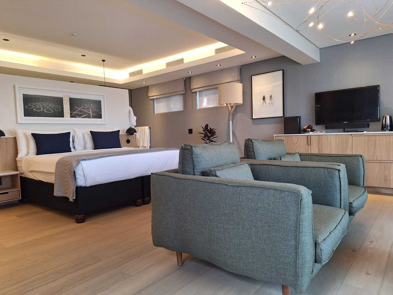 Quarto de hotel moderno com cama, área de estar e televisão de tela plana.