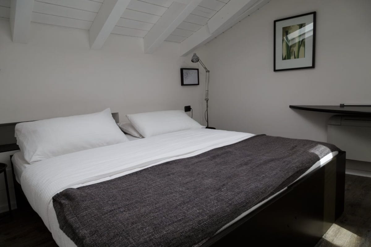 Um quarto com uma cama, uma escrivaninha e uma luminária.
