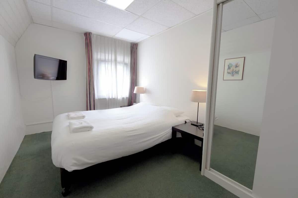 Quarto de hotel com cama, televisão, candeeiro e espelho.