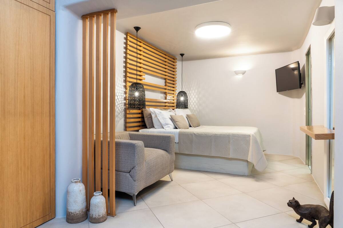 Quarto compacto com duas camas, um separador de madeira e uma televisão na parede.