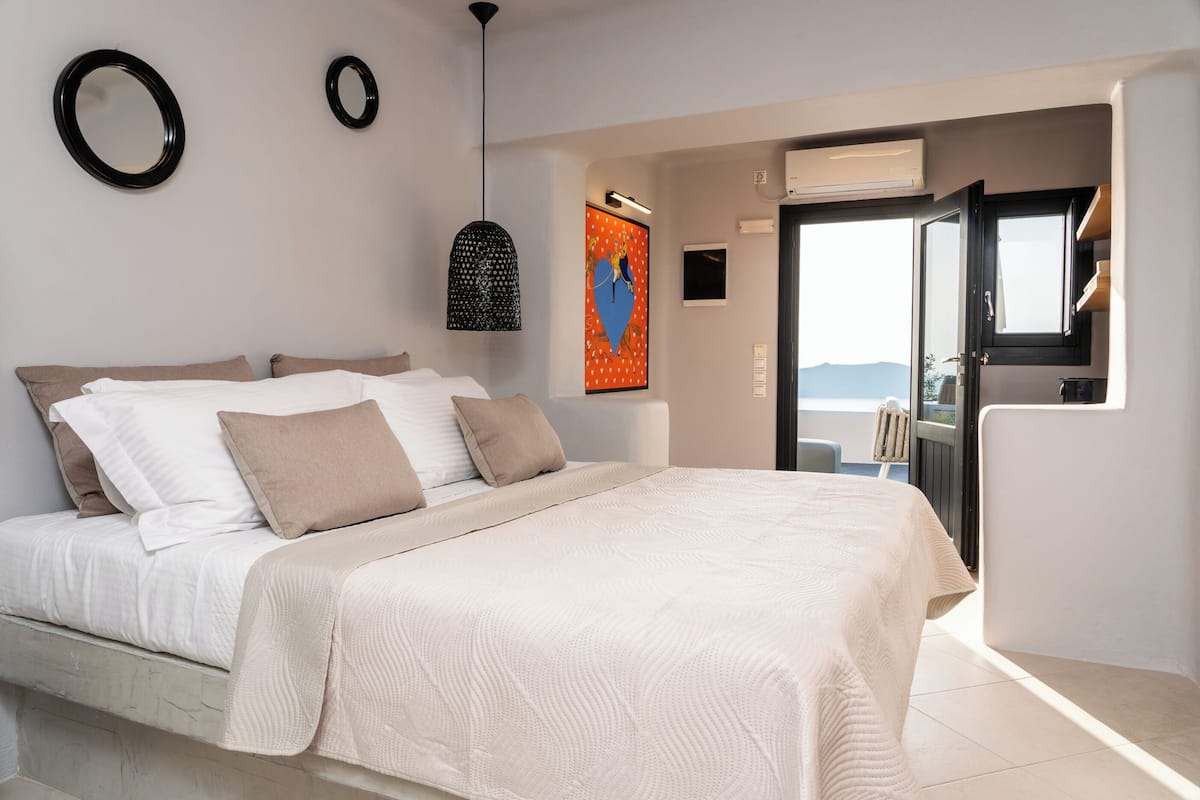 Um quarto com cama, luminária pendente, espelho fixado na parede e porta que dá para área externa.