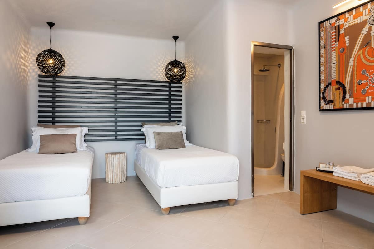 Quarto moderno com duas camas de solteiro, um banco de madeira, chuveiro e uma obra de arte emoldurada na parede.
