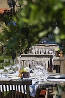 Restaurante com mesas e cadeiras de madeira ao ar livre, com copos de vinho e pratos vazios.