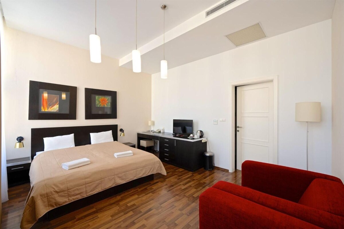 Quarto de hotel com cama, escrivaninha com computador, cadeira e obra de arte na parede.