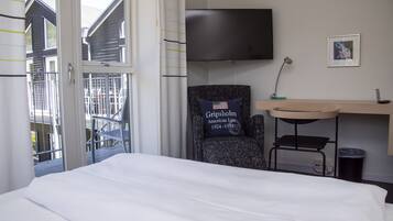 Quarto de hotel com cama, uma cadeira com travesseiro da bandeira americana, escrivaninha e televisão na parede.