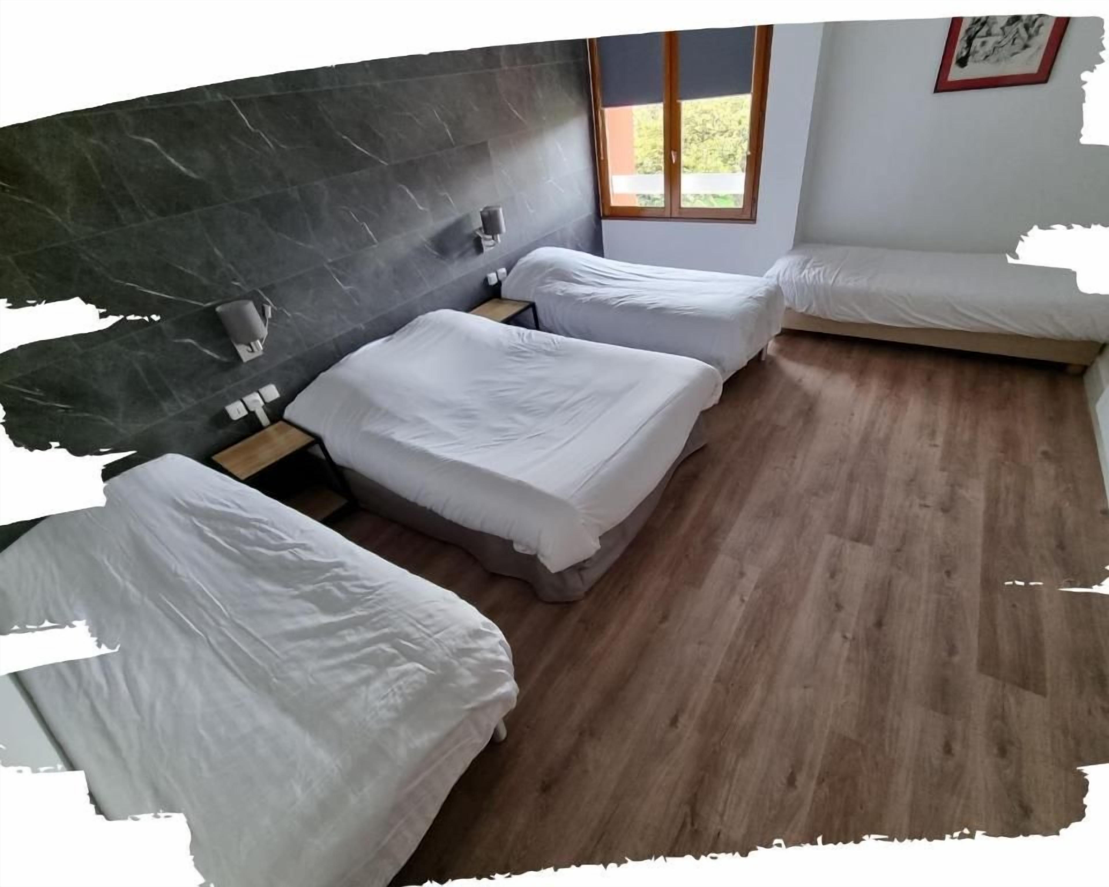 Quarto com duas camas, parede escura, janela e piso de madeira.