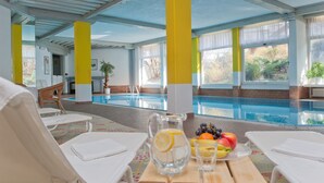 Uma área à beira da piscina com espreguiçadeiras, uma mesa com frutas e um jarro de água, e vista para a piscina.