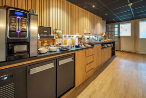 Uma cozinha moderna com máquina de café integrada, geladeira e bancada de café da manhã com diversos alimentos.