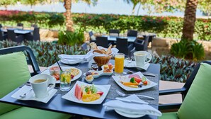 Uma área de refeições ao ar livre com mesas preparadas para o café da manhã, incluindo pratos de comida, bebidas e uma cesta de pão.