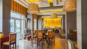 Um restaurante com móveis de madeira, luminárias de vime suspensas e um bar ao fundo.