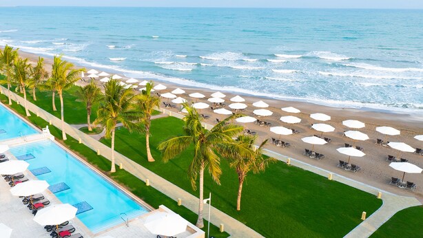 Resort com piscina, praia com guarda-sóis e palmeiras.