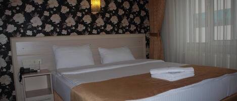 Quarto de hotel com uma cama grande, mesa de cabeceira com abajur e papel de parede floral.