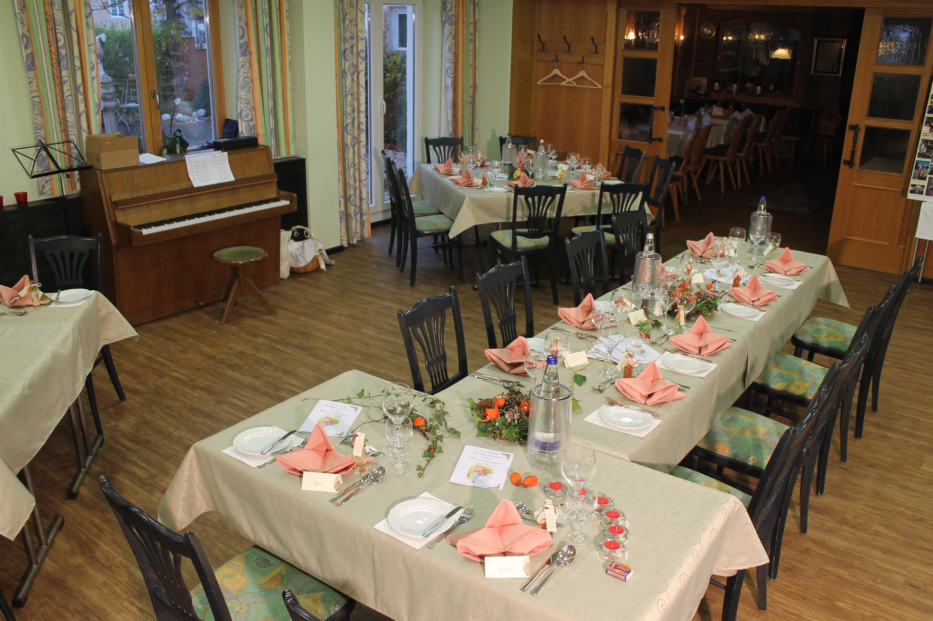 Uma sala de jantar com várias mesas postas para refeição, um piano e cadeiras com assentos acolchoados.