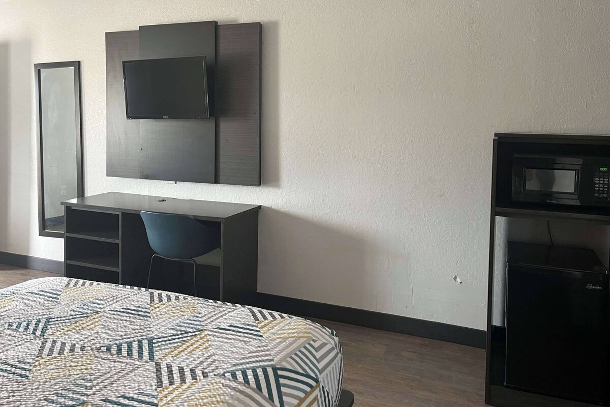 Quarto de hotel com uma cama, uma escrivaninha com cadeira, televisão de tela plana e micro-ondas.