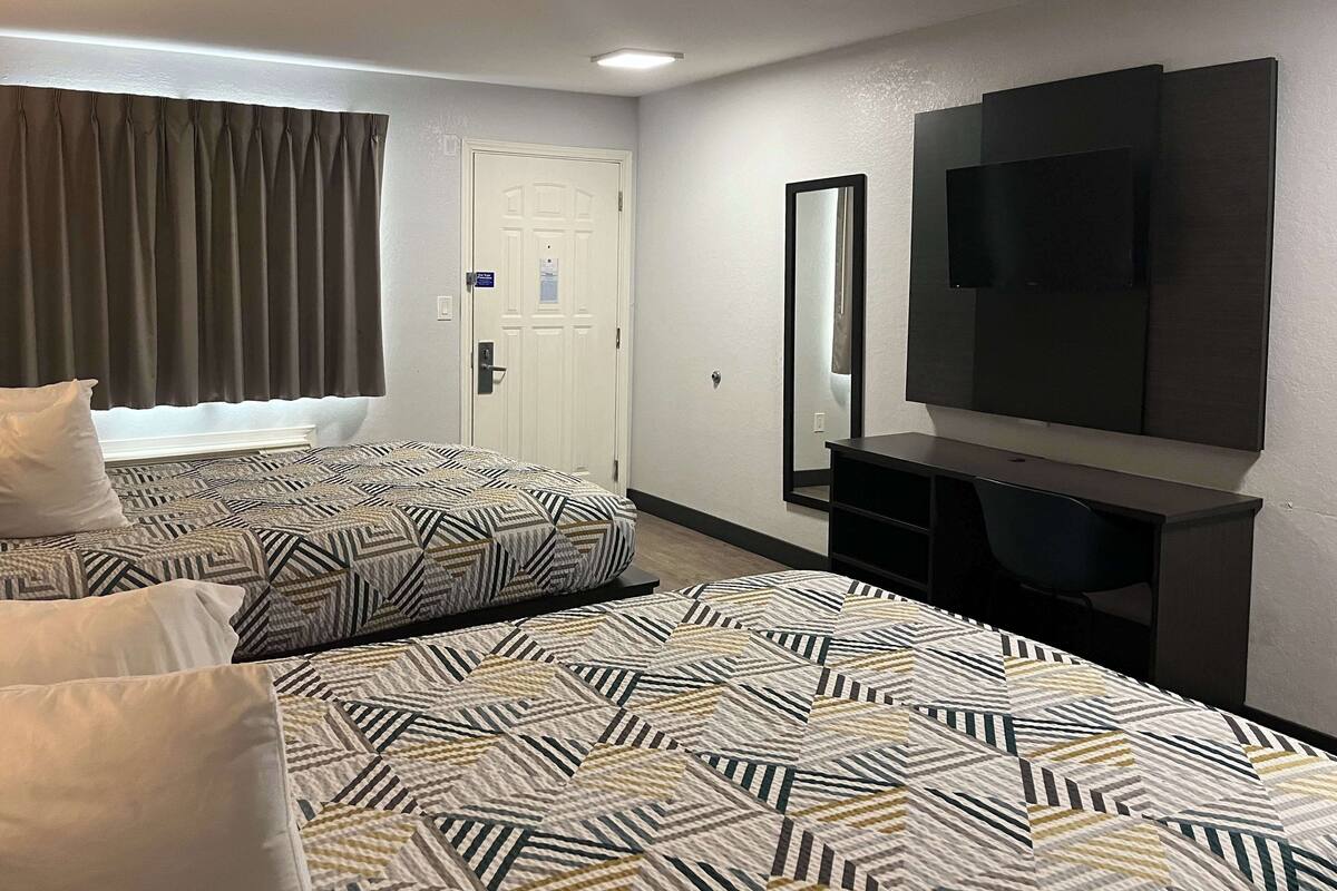 Quarto de hotel com duas camas, televisão, secretária e porta.