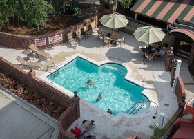 Piscina com borda de tijolos, cadeiras de sol e guarda-sóis.