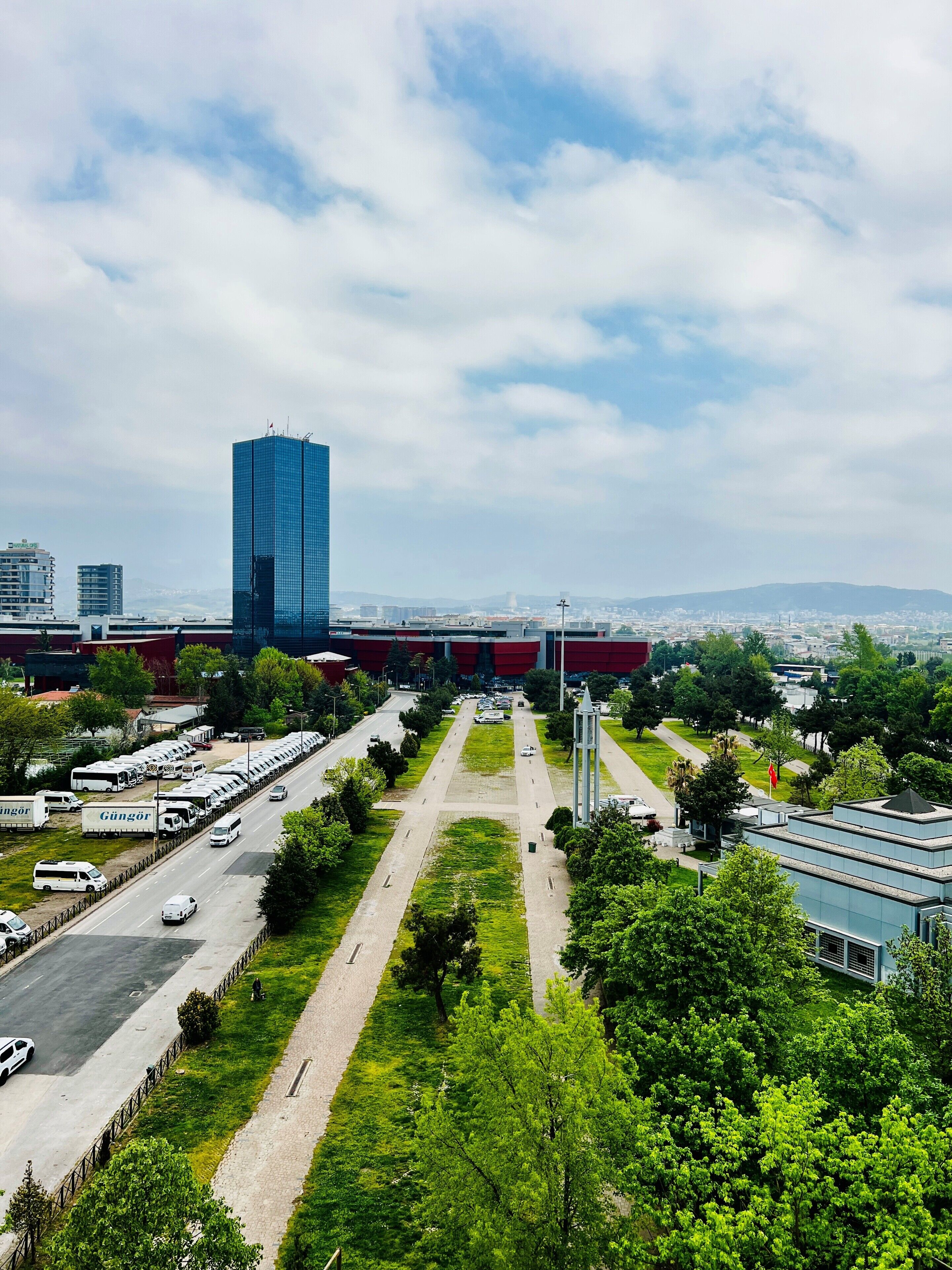 Paisagem urbana com um edifício moderno em destaque, um estacionamento com veículos recreativos e uma área verde do parque.