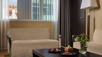 Quarto de hotel moderno com sofá, mesa de jantar com prato de comida, vaso com flores e luminária.