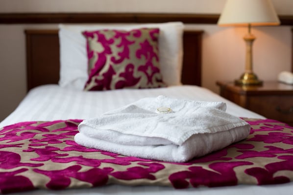 Cama bem arrumada com toalha branca, manta estampada e travesseiro decorativo.