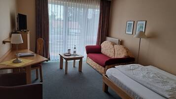 Quarto de hotel com cama, escrivaninha, cadeira, mesa pequena, sofá e janela com cortinas.