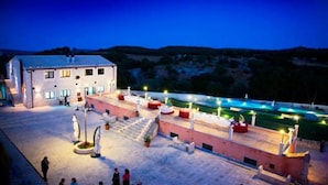 Um edifício com um pátio, degraus que levam a um terraço e uma área de piscina iluminada.