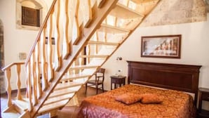 Um quarto com escada de madeira, cama com colcha estampada, mesa de cabeceira e quadro pendurado na parede.