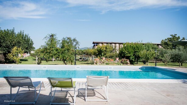 Uma piscina com três espreguiçadeiras, cercada por vegetação exuberante e um céu azul límpido.