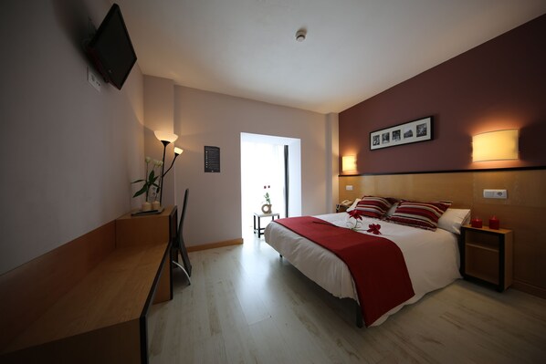 Quarto de hotel moderno com cama, mesa de cabeceira, abajur e secretária com cadeira.