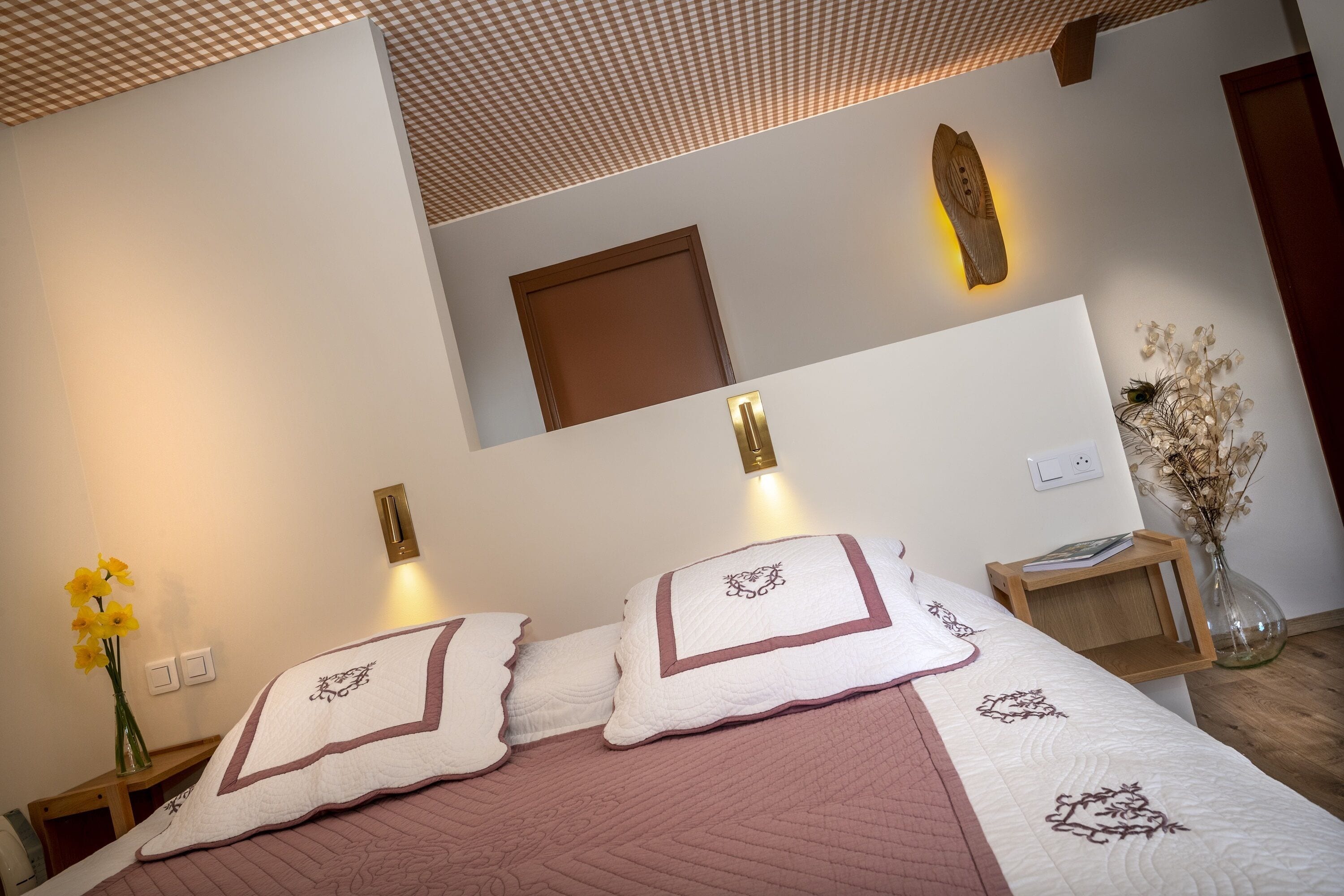 Quarto bem organizado com cama, mesas de cabeceira, espelho e luminária na parede.