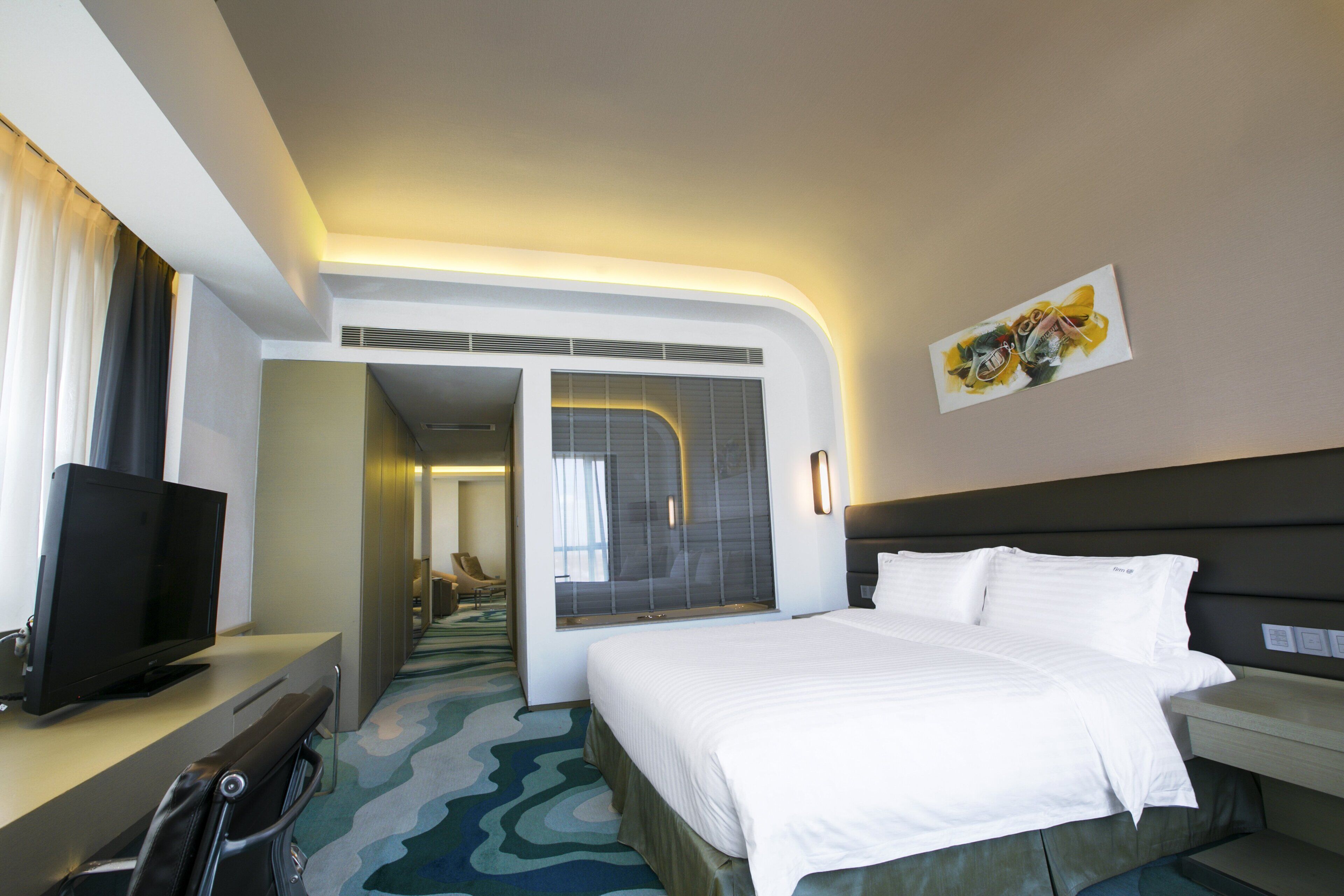 Quarto de hotel com cama, uma mesa com televisão, uma cadeira e porta de banheiro.