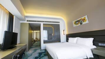Quarto de hotel com cama, uma mesa com televisão, uma cadeira e porta de banheiro.