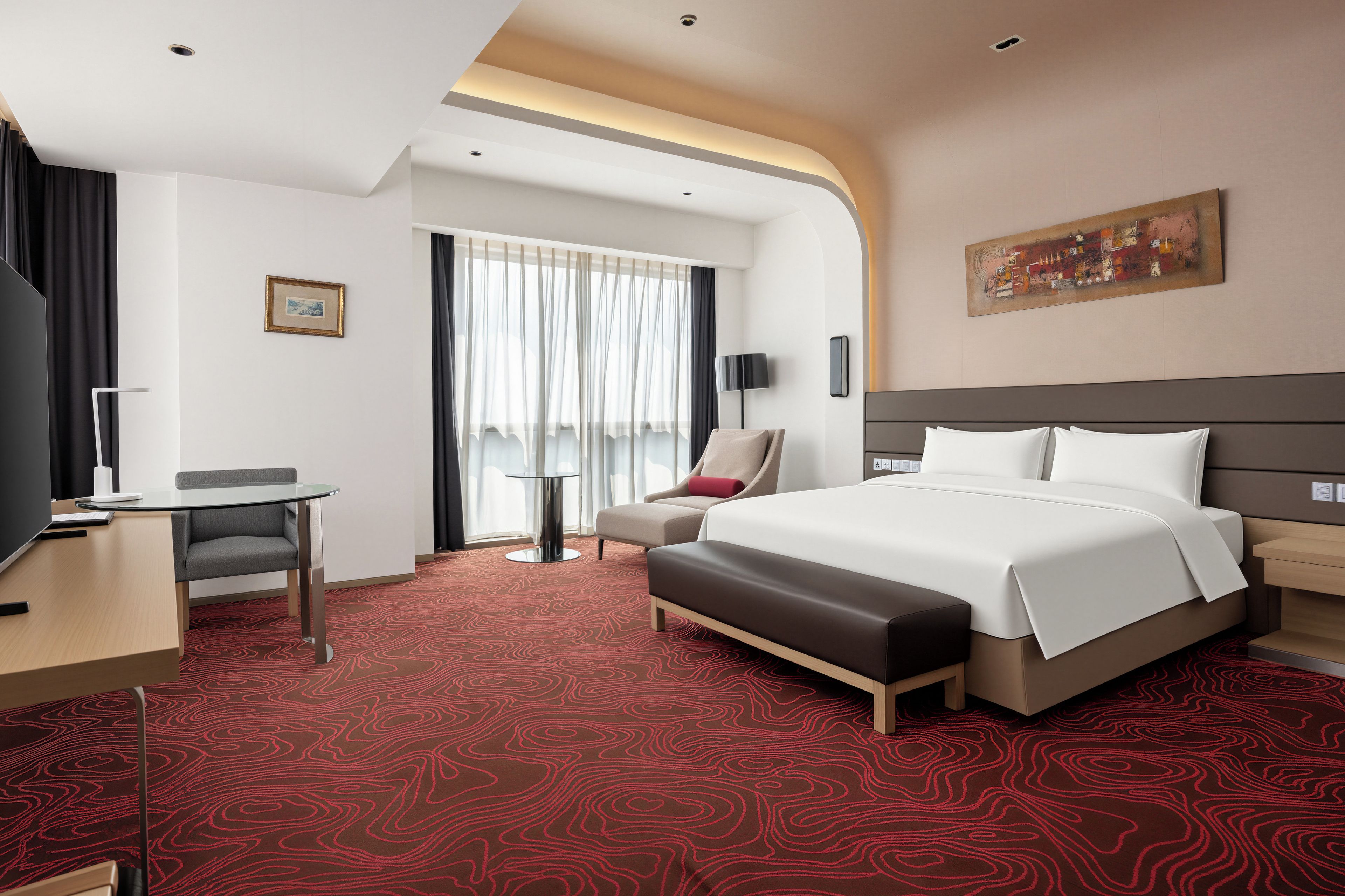 Quarto de hotel com cama, escrivaninha, cadeira, televisão e um quadro na parede.