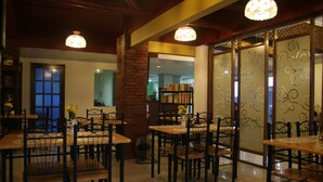 Um restaurante com mesas de madeira e cadeiras pretas, paredes de tijolo e painéis de vidro decorativos.