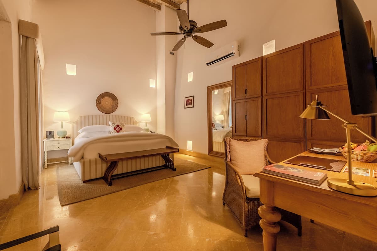 Um quarto espaçoso com uma cama grande, uma escrivaninha com luminária, um ventilador de teto e painéis de madeira.