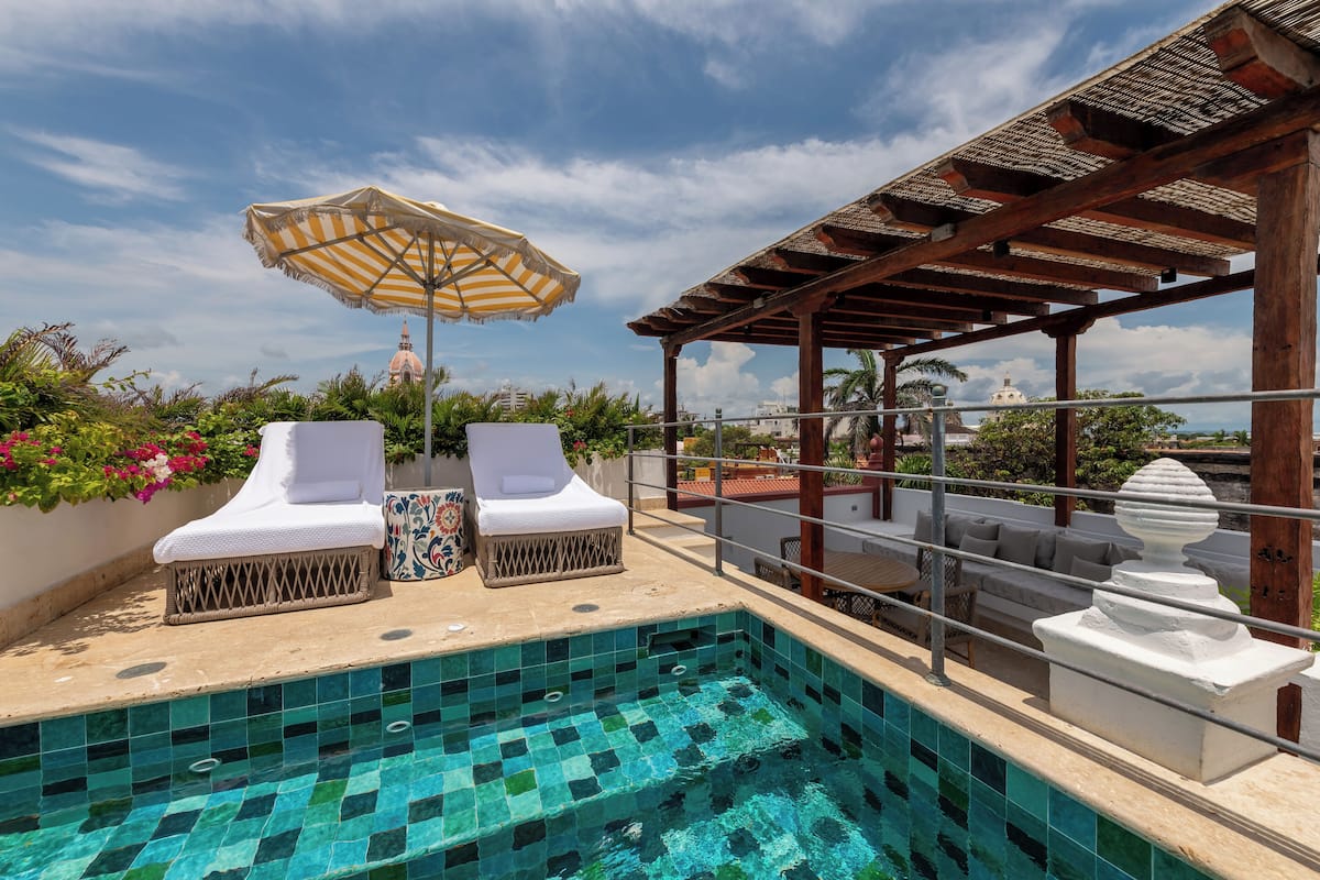 Uma área de piscina no terraço com espreguiçadeiras, um guarda-sol e vista para uma cúpula ao fundo.