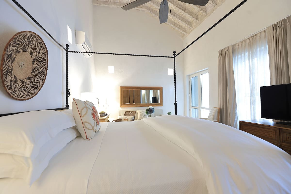Um quarto espaçoso com cama de dossel, um espelho grande, uma televisão de tela plana e uma janela com cortinas.