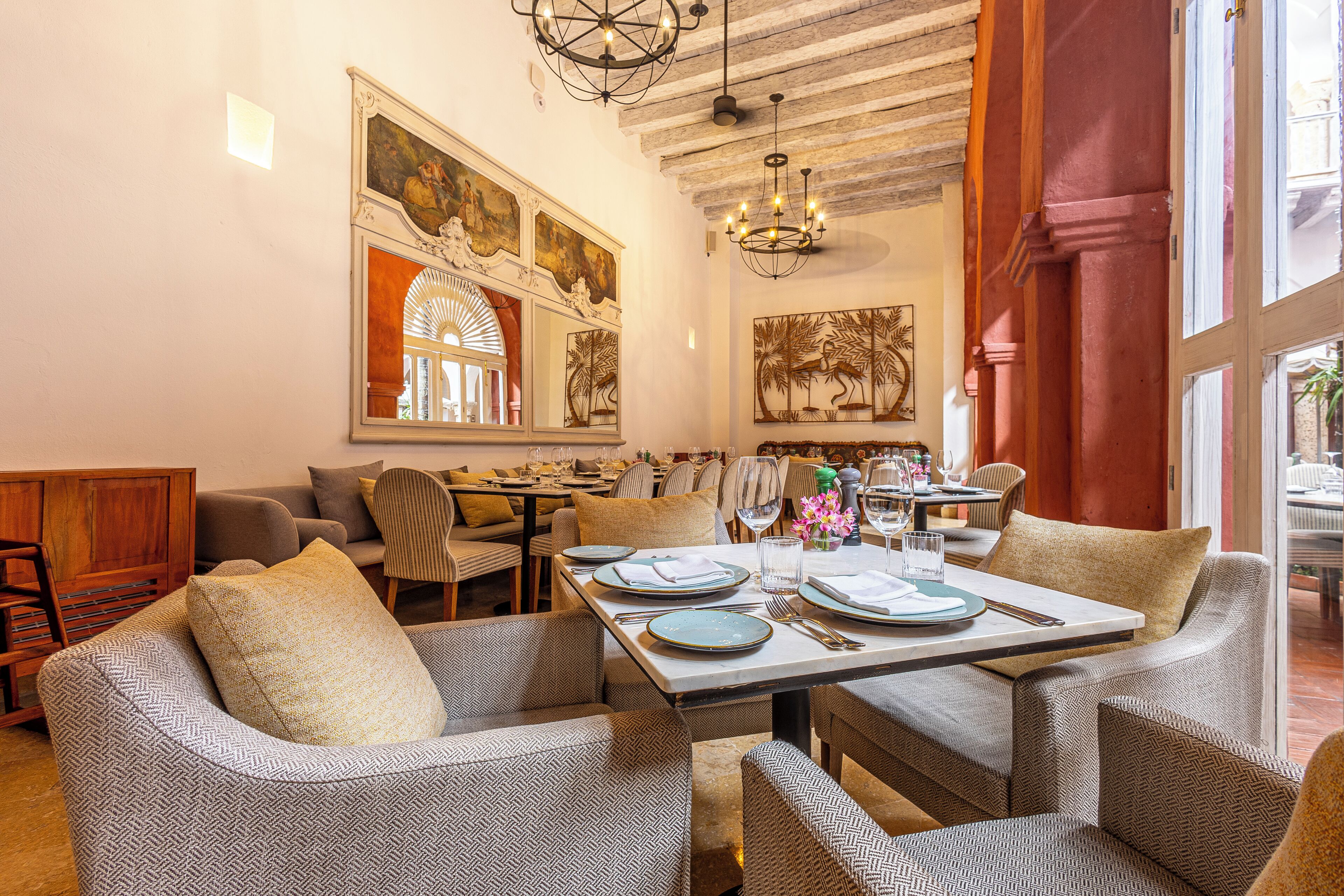 Uma sala de jantar com várias mesas e cadeiras, quadros grandes nas paredes e um lustre.