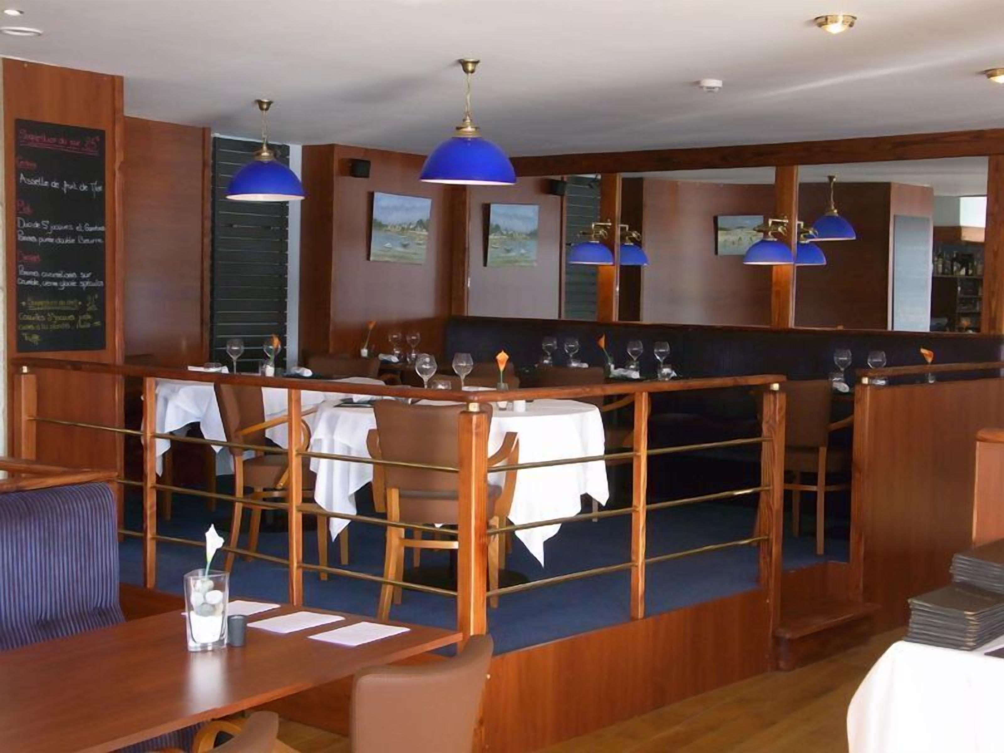 Restaurante com mobiliário de madeira, luminárias pendentes azuis e um cardápio em lousa.