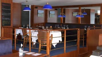 Restaurante com mobiliário de madeira, luminárias pendentes azuis e um cardápio em lousa.