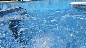 Piscina com água azul cristalina, rodeada por palmeiras e espreguiçadeiras.