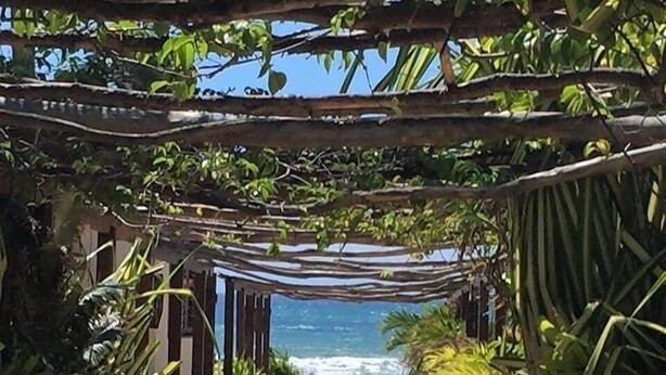 Um caminho que leva a uma praia, com uma pérgula de madeira acima.