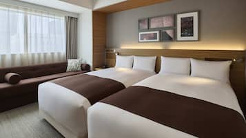 Quarto de hotel com duas camas, um sofá e uma janela grande com cortinas.
