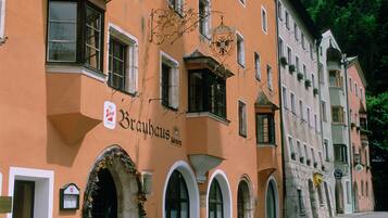 Um edifício com a placa 'Brauhaus', indicando que se trata de uma cervejaria. Possui várias janelas, algumas com toldos, e uma entrada em arco de pedra.