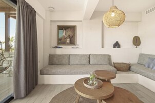 Uma sala de estar moderna com um sofá cinzento, uma mesa redonda de madeira, uma luminária pendente de vime e um quadro na parede.
