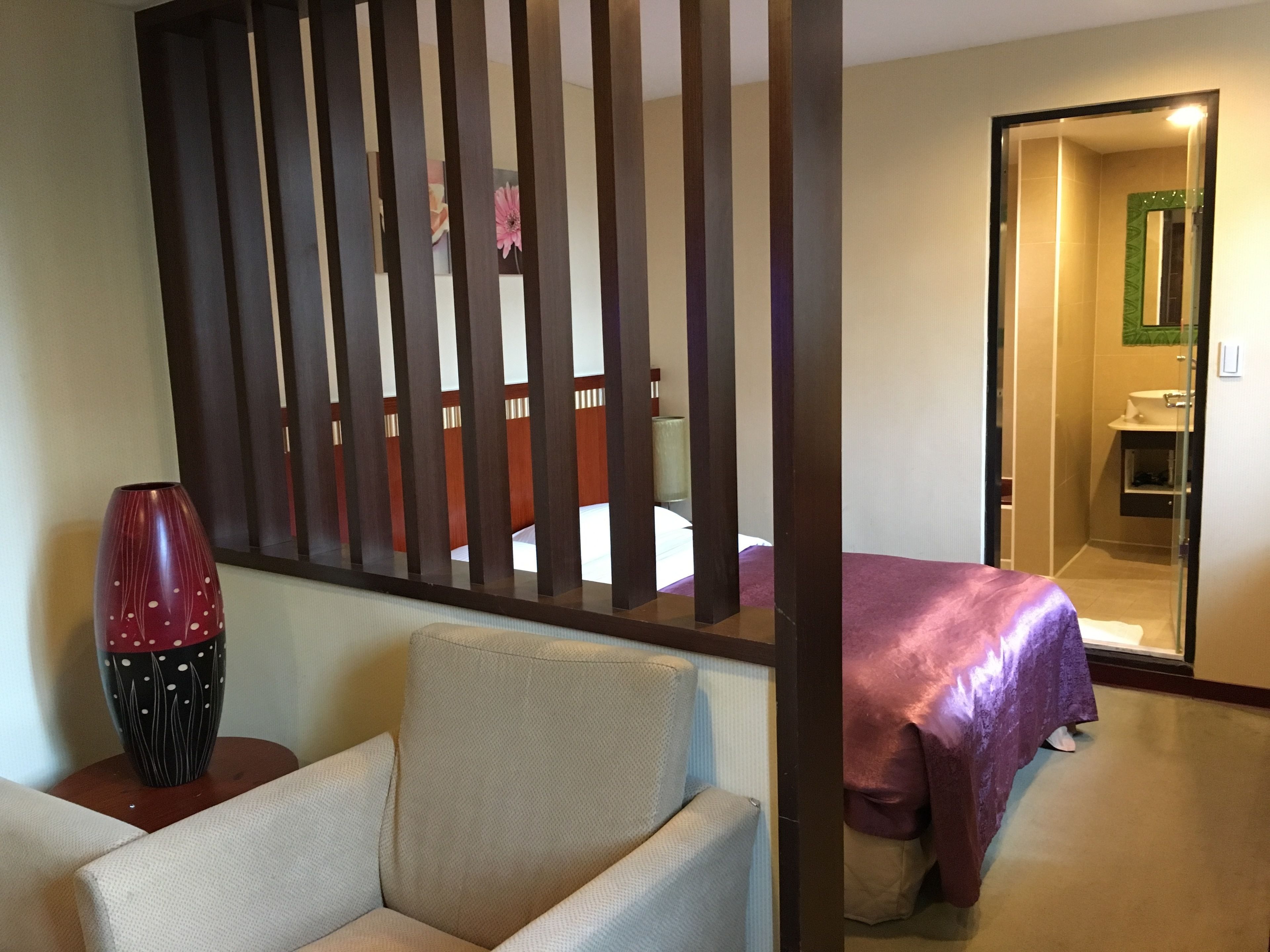 Quarto de hotel com uma cama, uma cadeira, um vaso decorativo e um divisória.