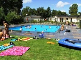 Piscina cercada por grama, com algumas pessoas na água e outras na beira da piscina.