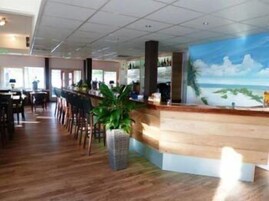 Uma área de bar com piso de madeira, um balcão com um mural de uma praia e algumas cadeiras.
