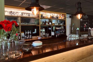Uma área de bar com prateleiras de garrafas de bebidas, copos e balcão com um vaso de flores vermelhas.