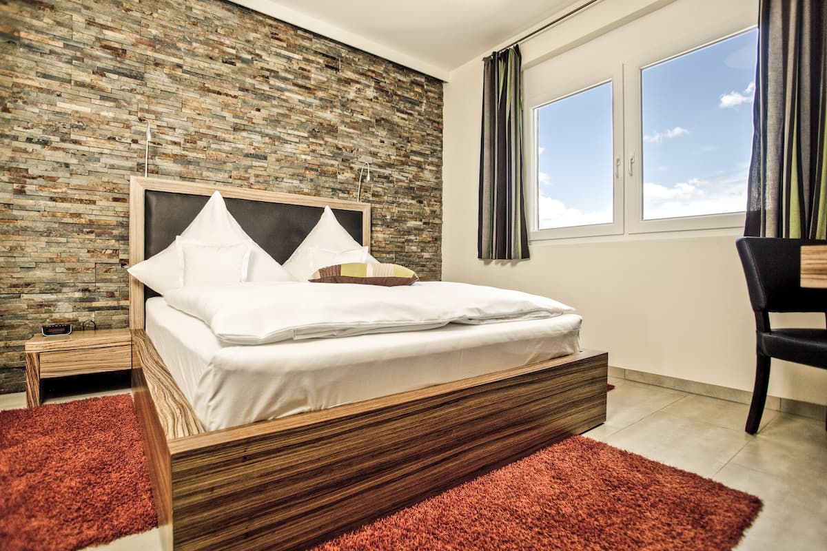 Quarto moderno com cama de madeira, parede de tijolos e uma grande janela.