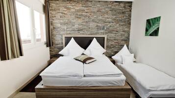 Quarto de hotel com parede em tijolos, uma cama grande com roupa de cama branca, duas mesas de cabeceira e uma janela com cortinas.
